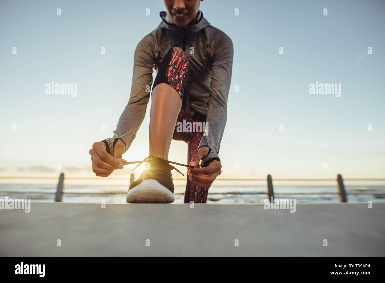Woman lacing running shoes before workout outdoors. Female runner tying her shoe laces while ...