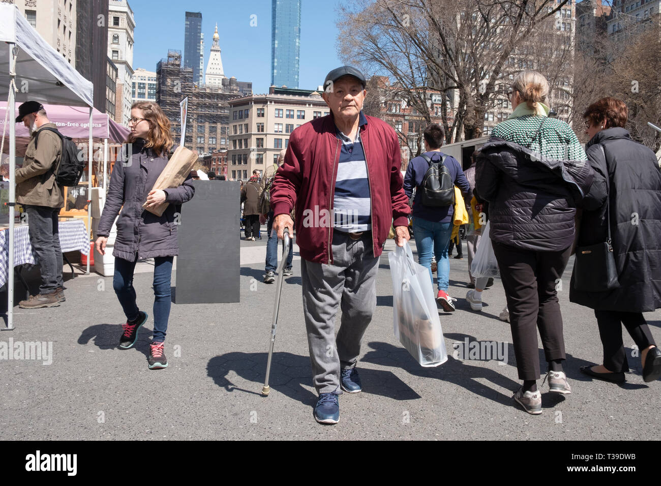 An older man with a cane & shopping bag walks through the Union Square ...