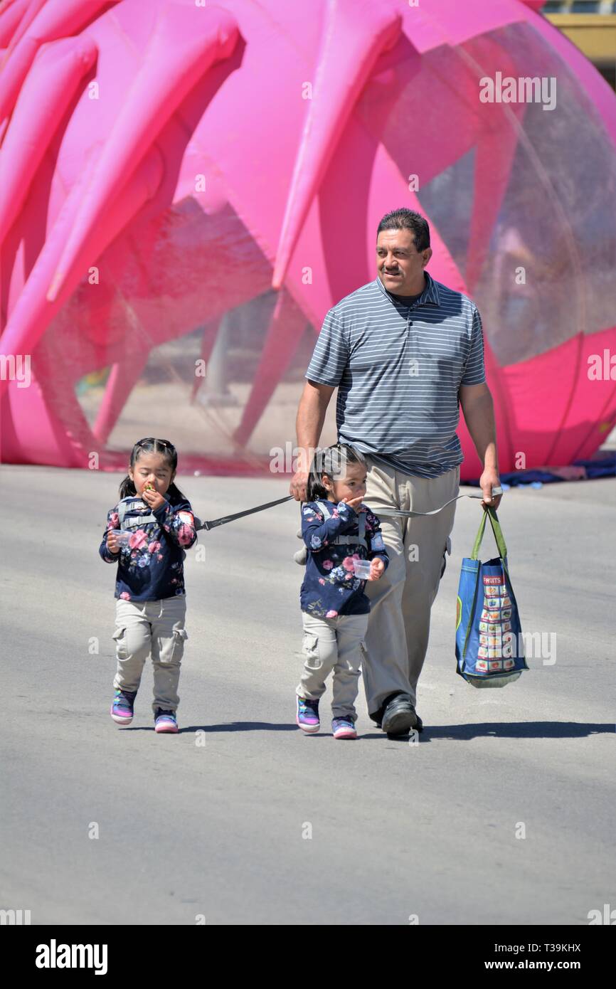 Father and his twin girls walking at public city event using a leash to ...