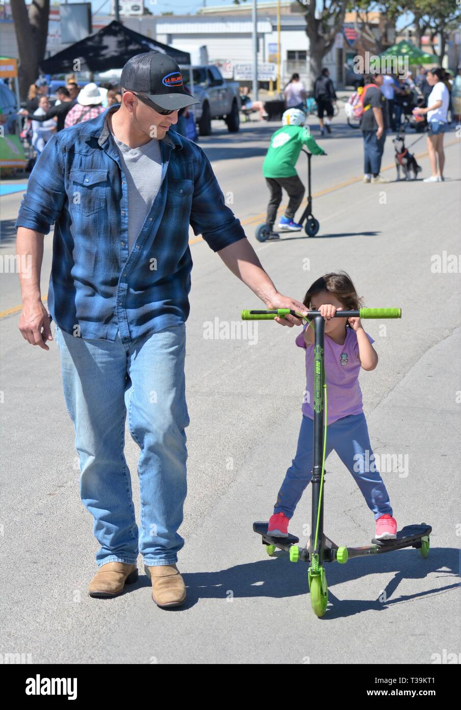 Father helping daughter learn how to use a skate board on open city ...
