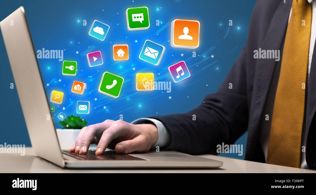Businessman hand typing on laptop with flying application icons around ...