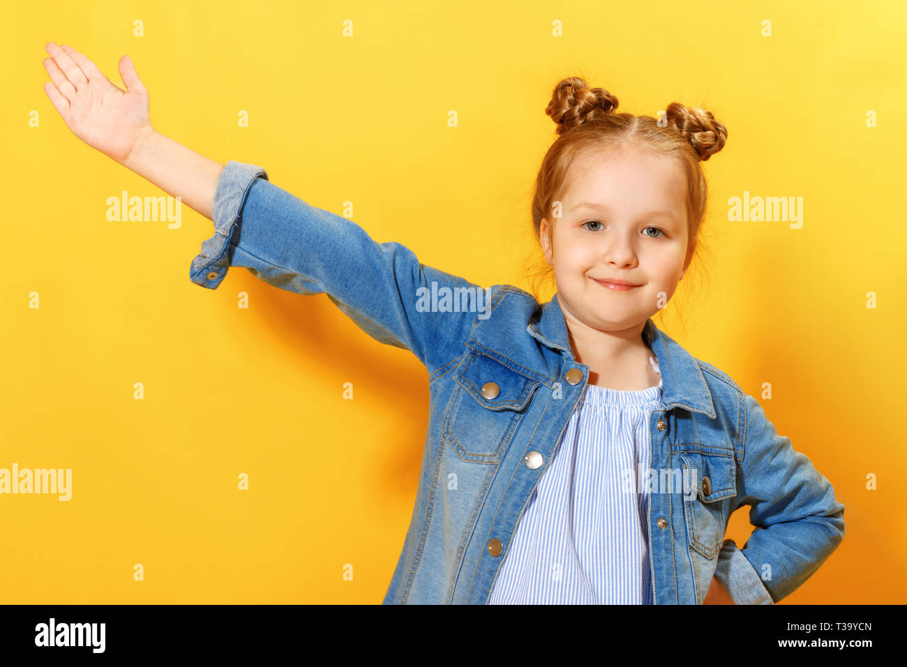 Closeup portrait of a cute attractive little girl on yellow background. The child points his ...