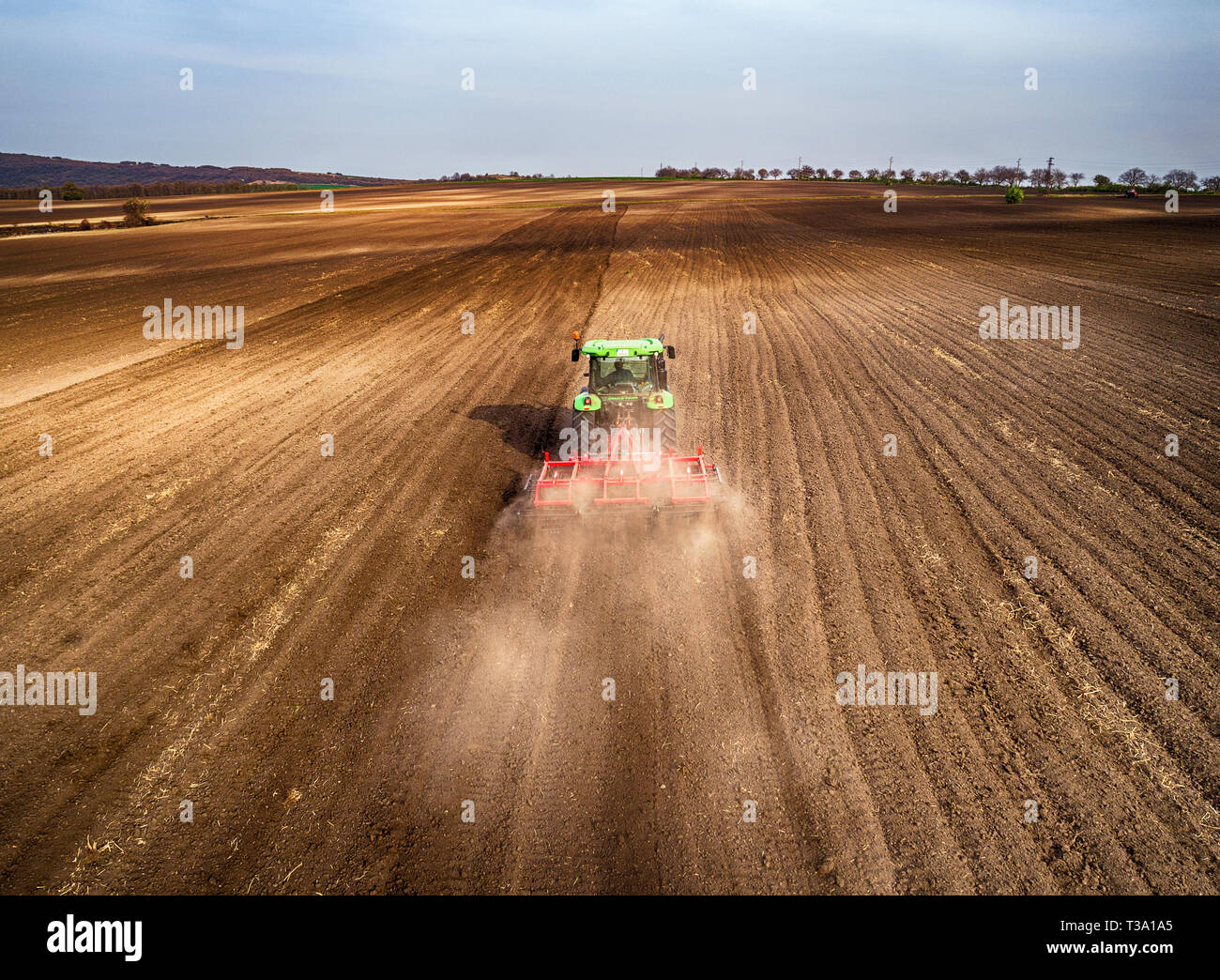 A Farmer On A Red Tractor With A Seeder Sows Grain In Plowed Land In A a-farmer-on-a-red-tractor-with-a-seeder-sows-grain-in-plowed-land-in-a