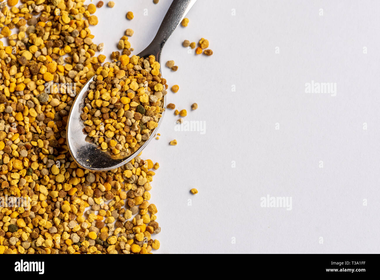granules of bee pollen on a sheet of white paper with a teaspoonful of ...