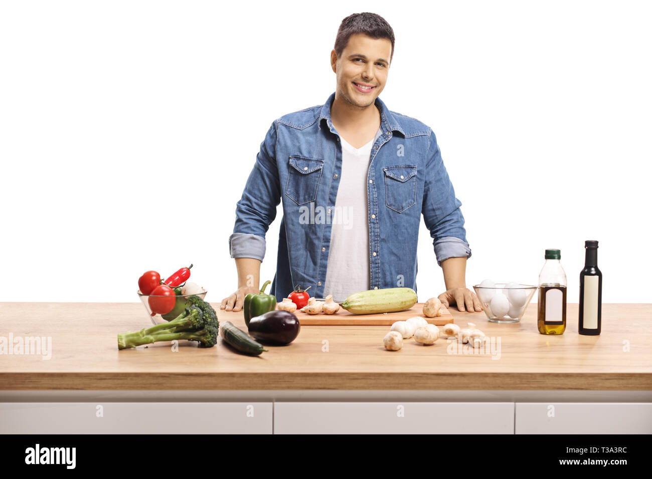 Smiling young guy cooking with healthy ingredients on a wooden counter ...