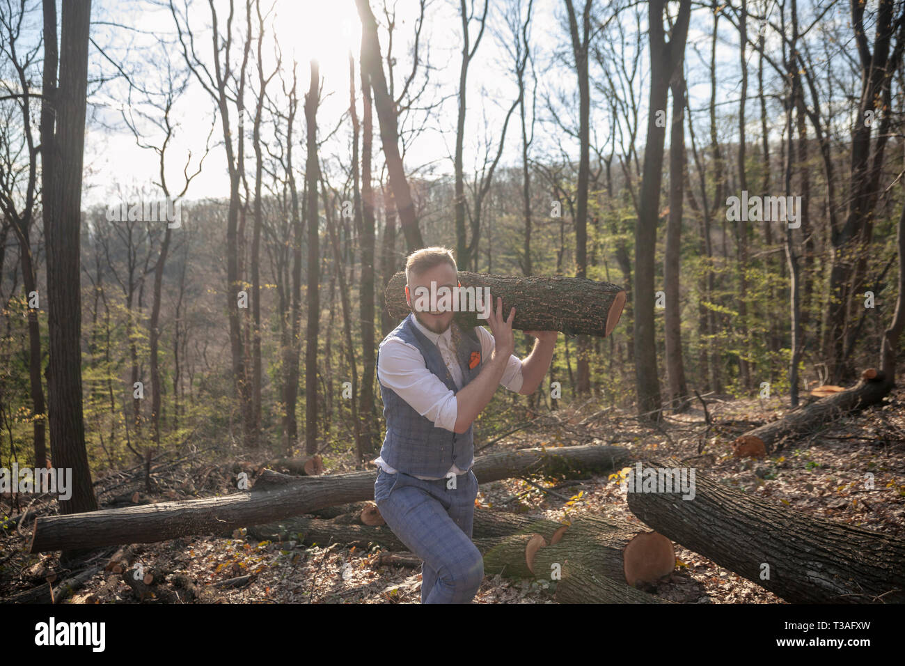 one young smiling man, dressed in suit, carrying wood log on his ...