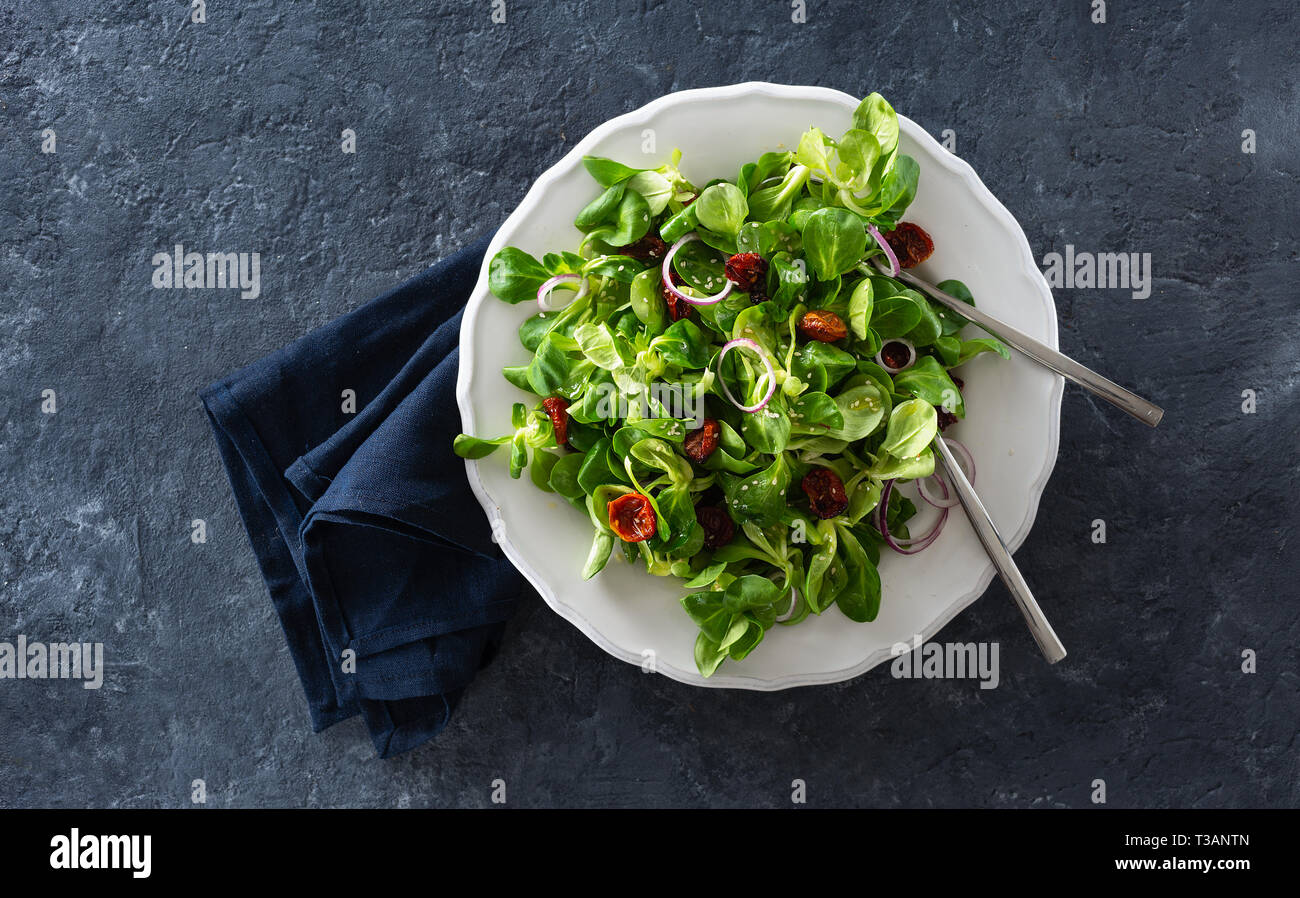 Bowl salad of green mache leaves and baked tomatoes on dark stone ...