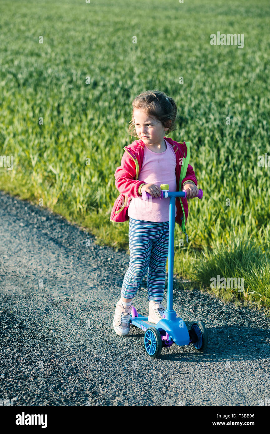 Little adorable girl having fun riding on scooter, playing outdoors ...