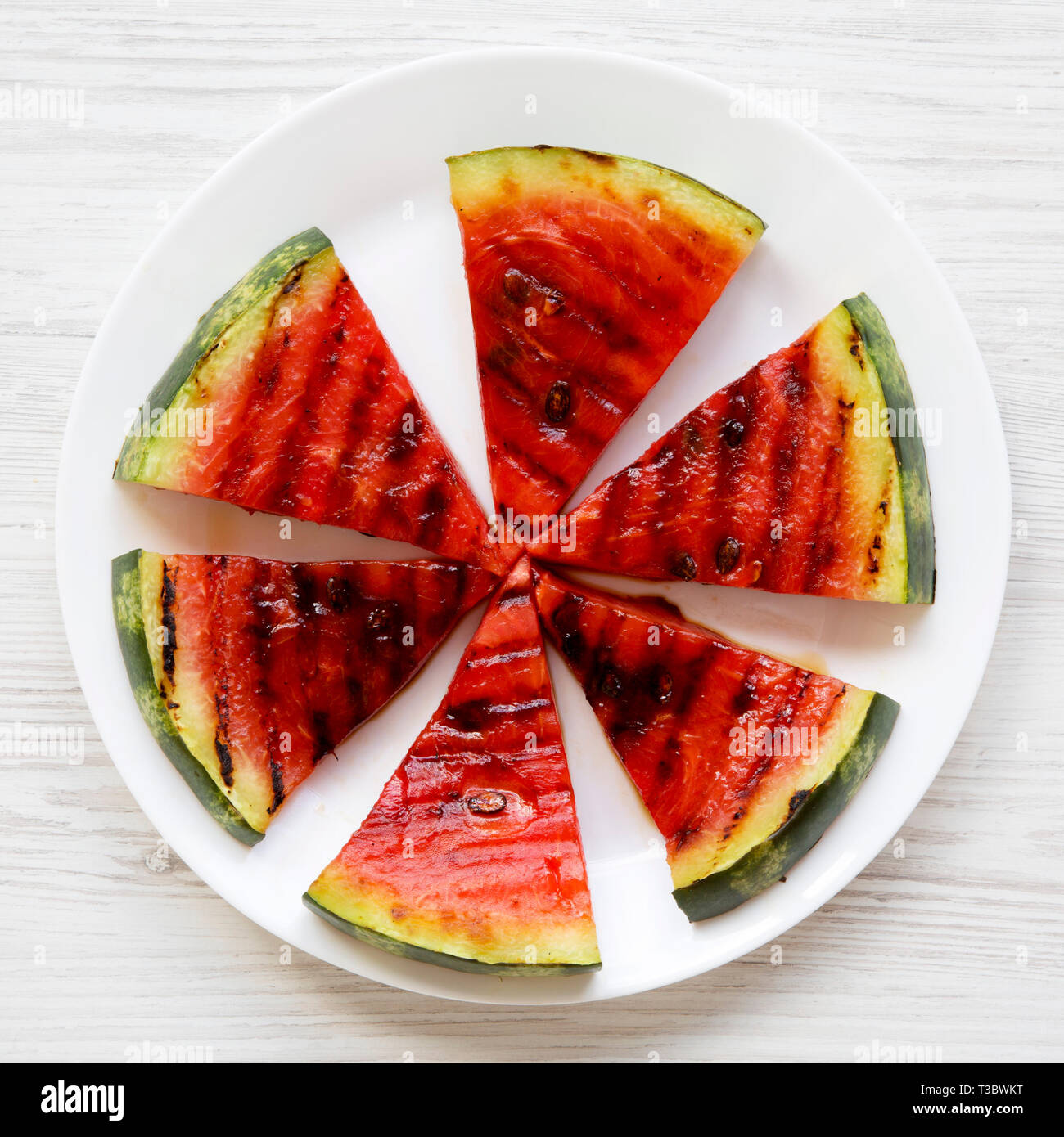 Many slices of fresh ripe grilled watermelon on a white round plate over white wooden surface ...
