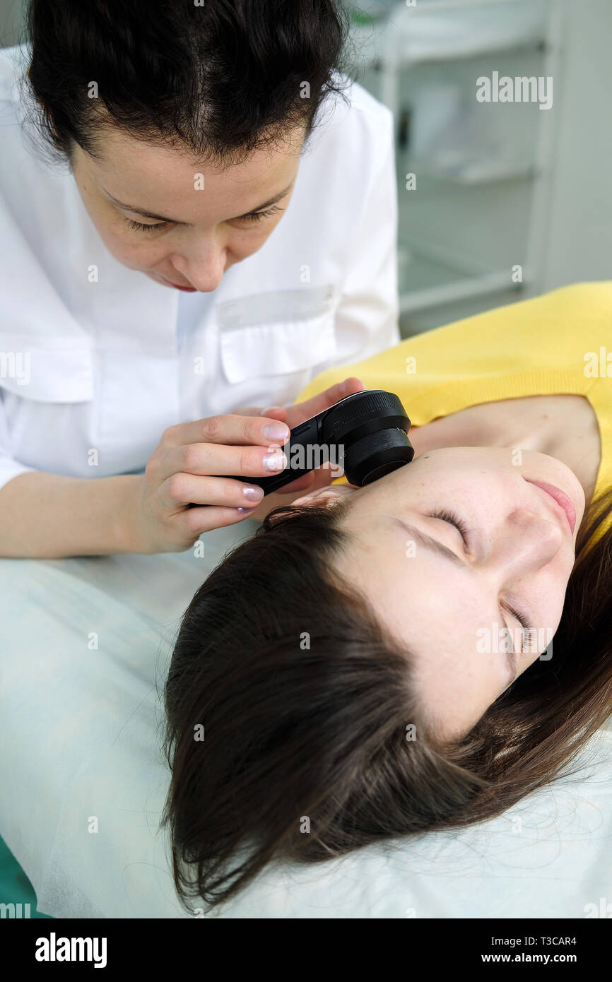 Female dermatologist using a professional dermatoscope while doing skin ...