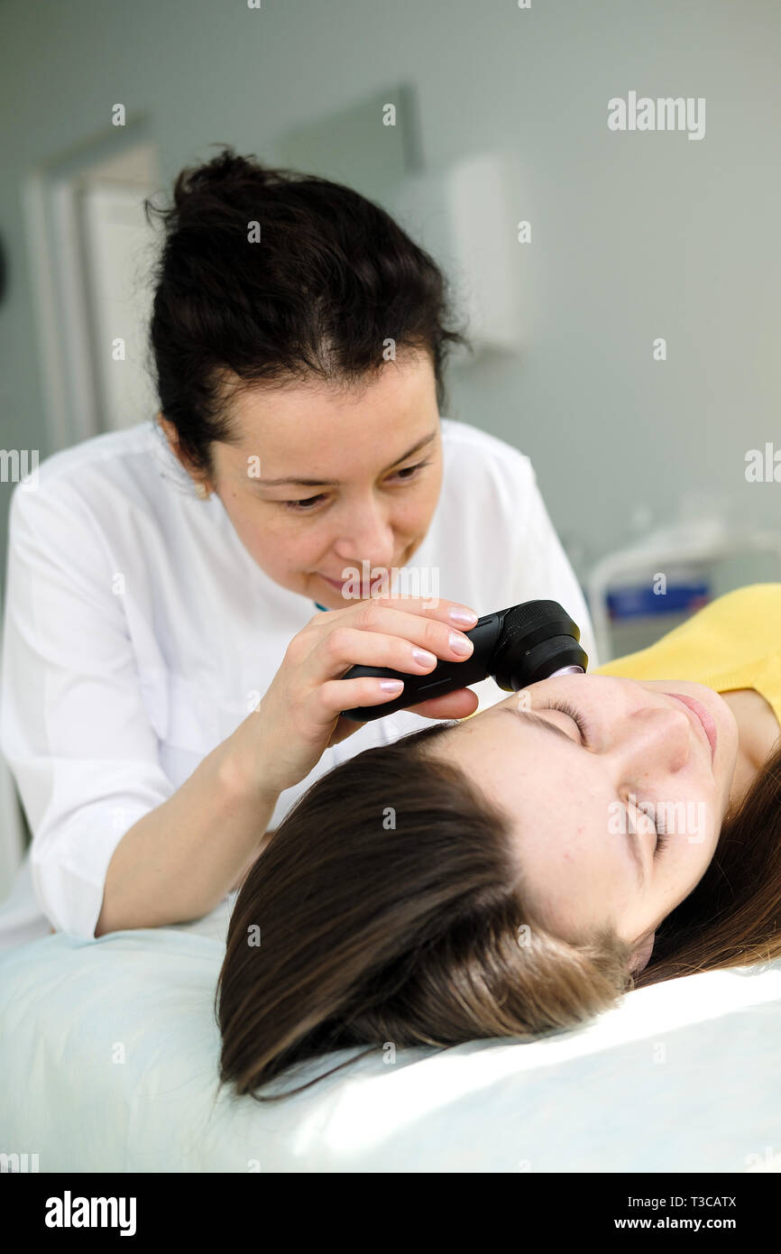 Female dermatologist using a professional dermatoscope while doing skin ...