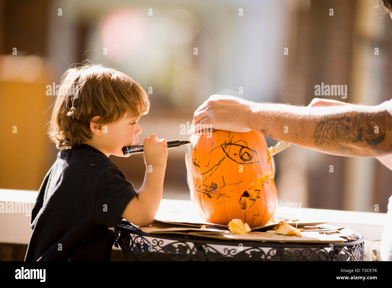 Father and son drawing face on pumpkin and carving Jack O' Lantern ...