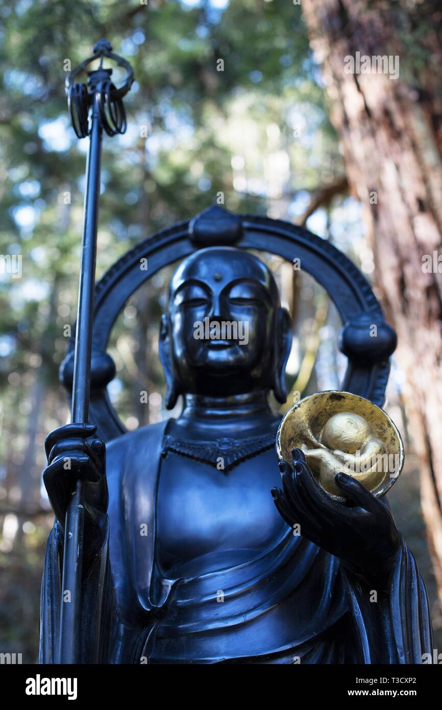 A black statue of Buddhist holding golden fetus, in Okunoin cemetery in ...