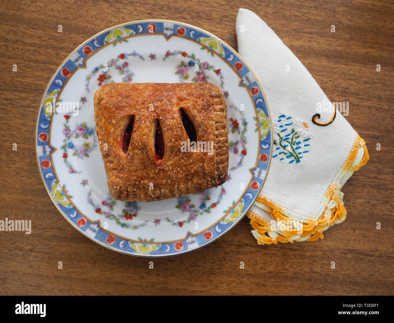 A raspberry filled pastry served on a china plate with blue rim and an ...