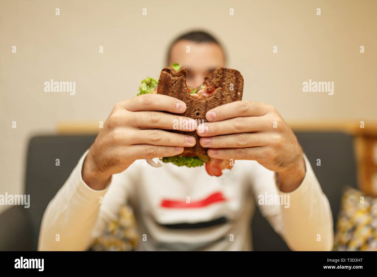 Closeup funny blurred protrait of young man hold bitten sandwich by his ...