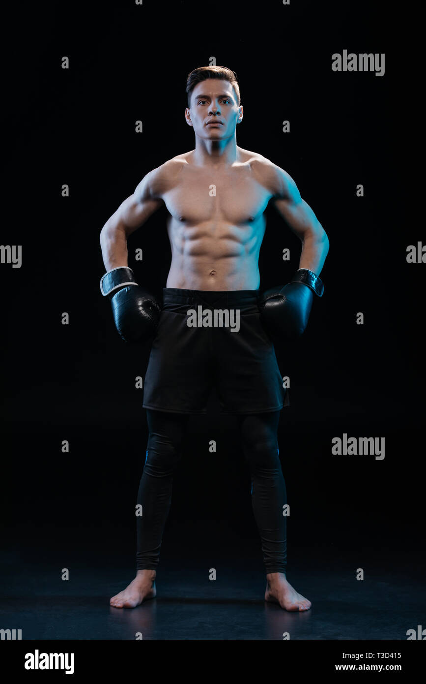 confident muscular barefoot boxer in boxing gloves posing on black ...