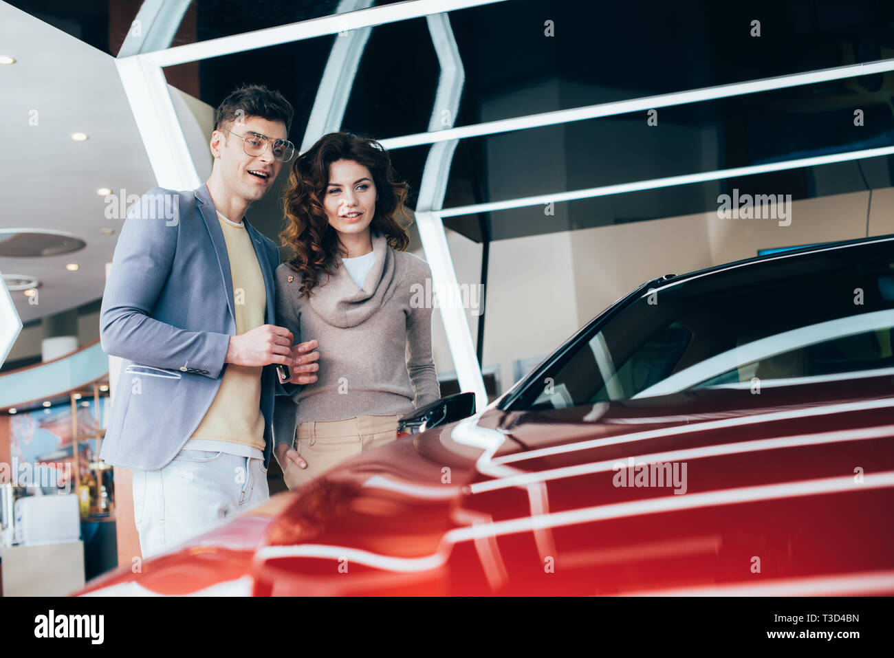 cheerful man holding keys while standing with curly girl near red ...