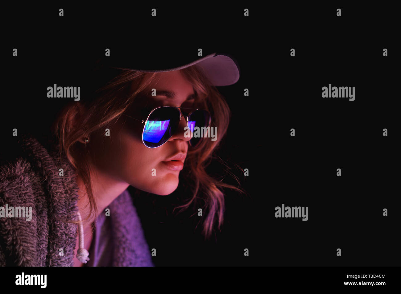 Hacker girl in a cap and sunglasses in front of a computer in neon ...