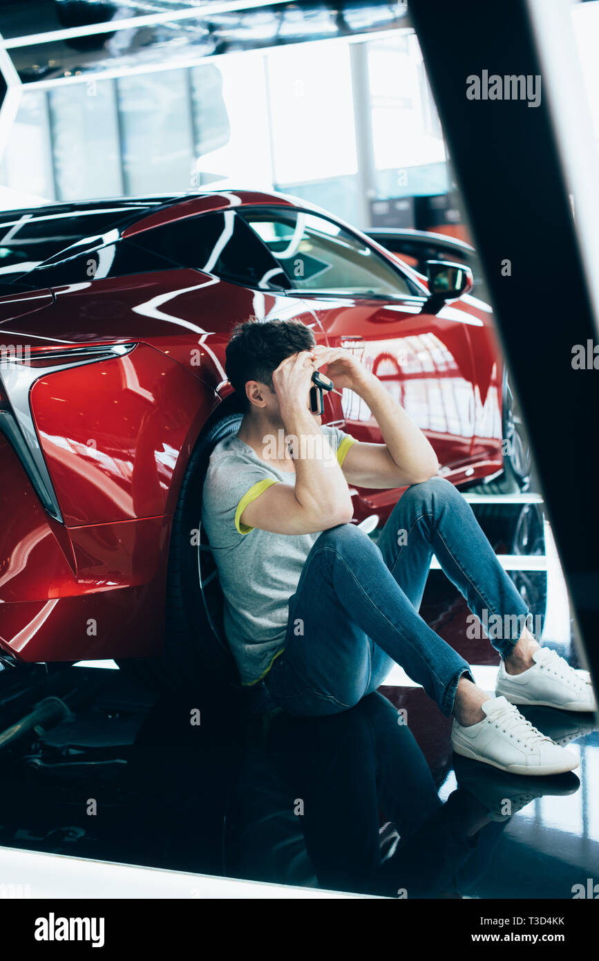 upset man sitting near red automobile in car showroom Stock Photo - Alamy