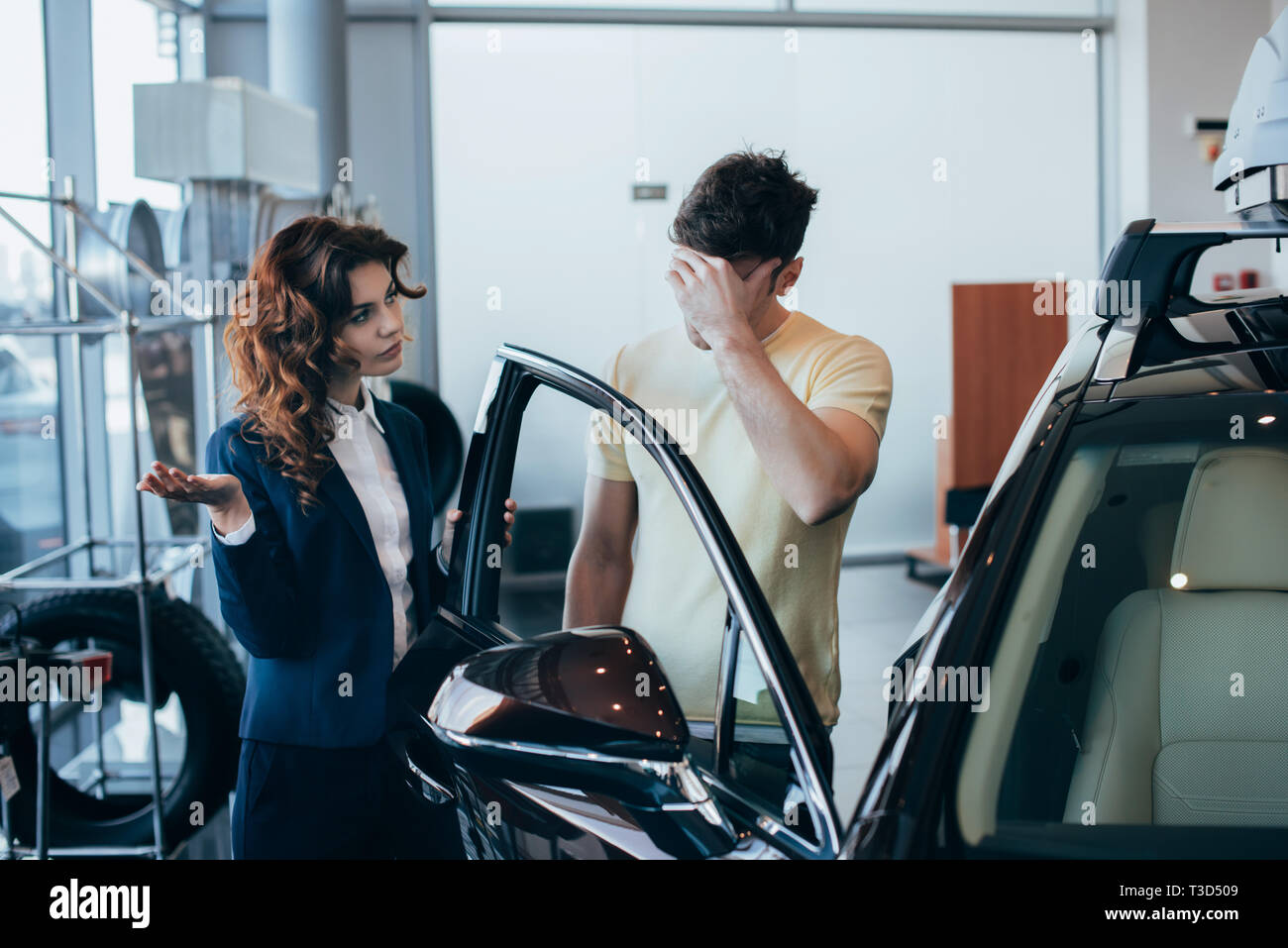 pretty car dealer and man holding hand on face standing near new car ...