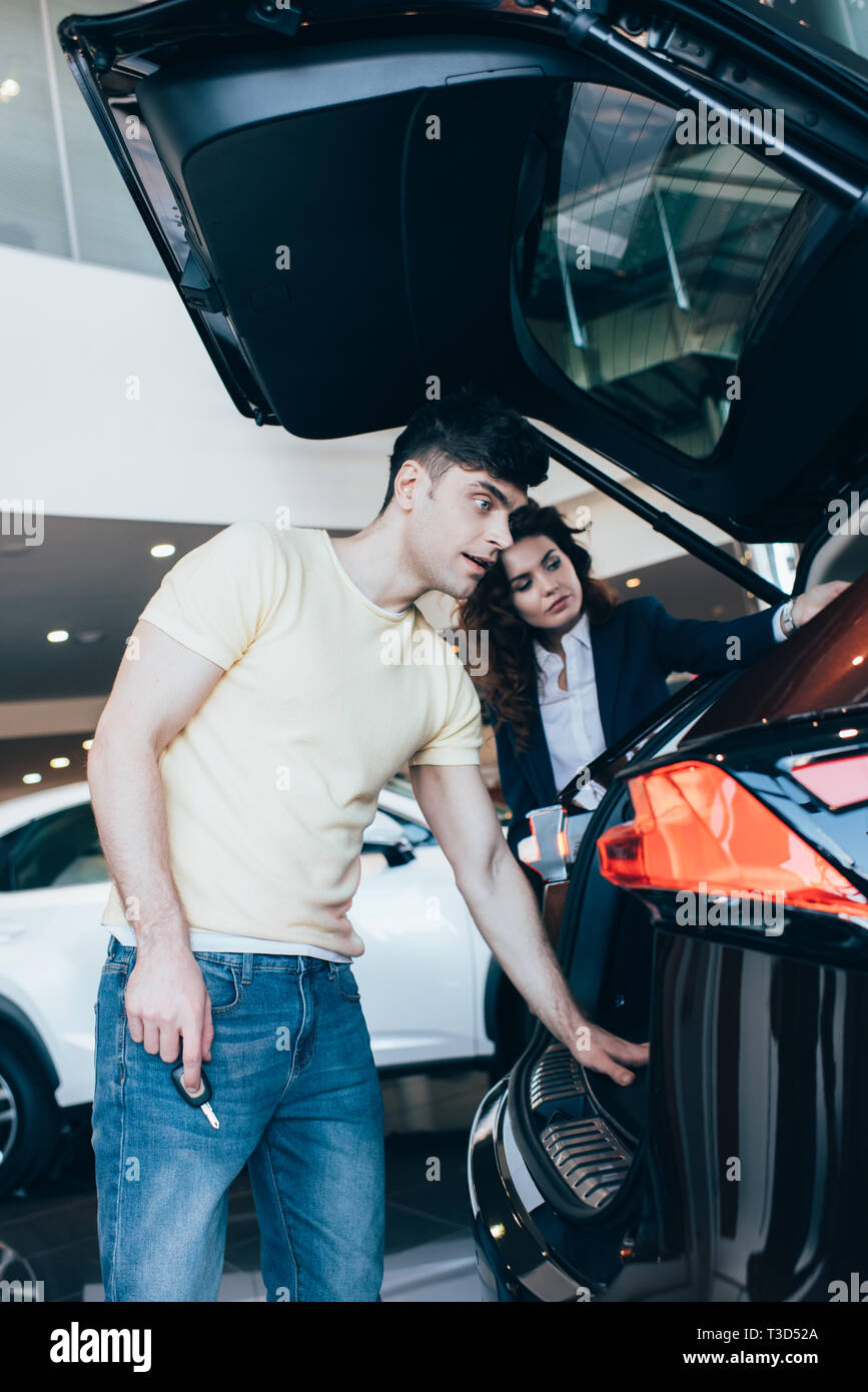 selective focus of handsome man and car dealer standing near new car ...