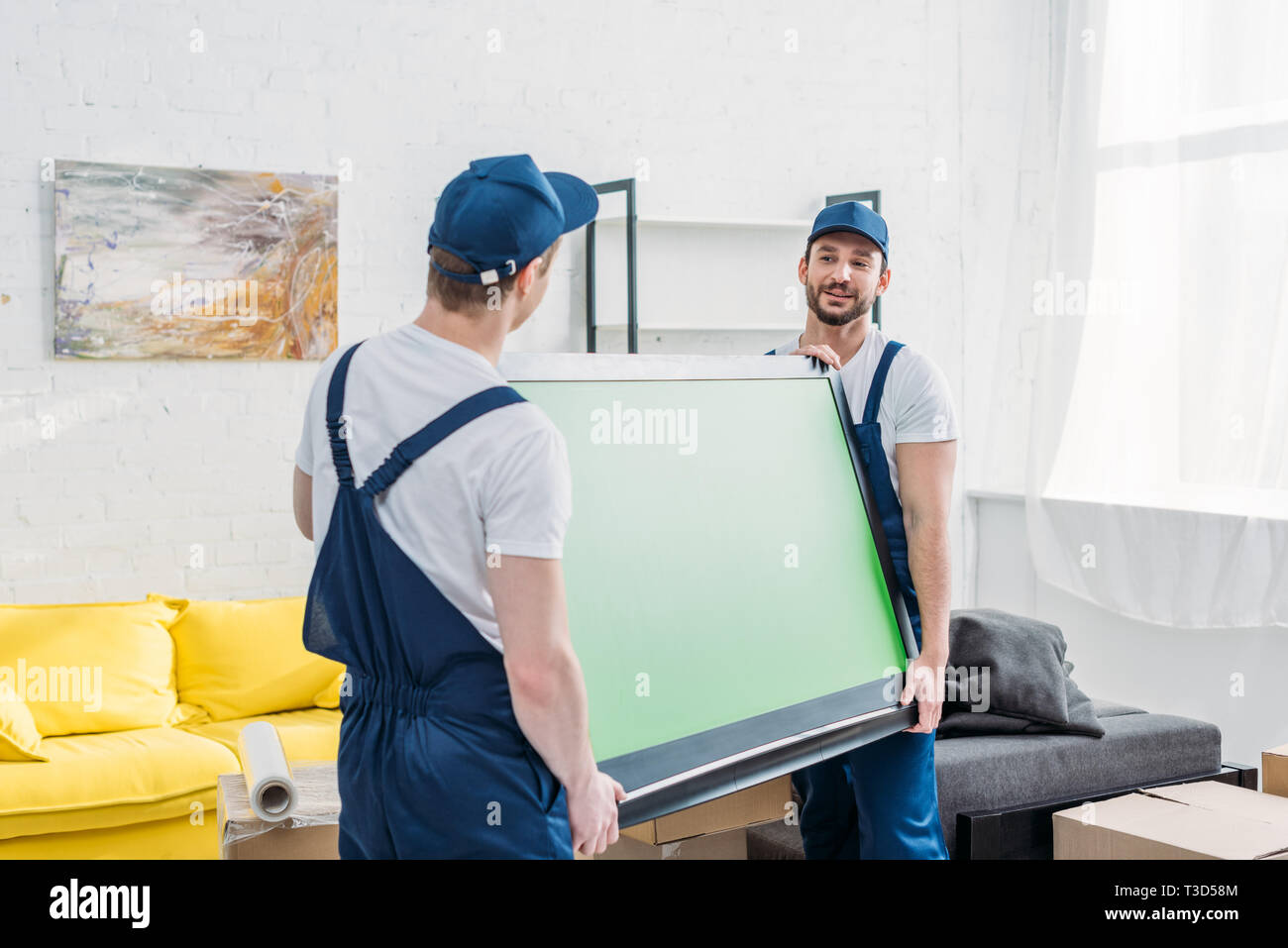 two movers in uniform transporting tv with green screen in living room ...
