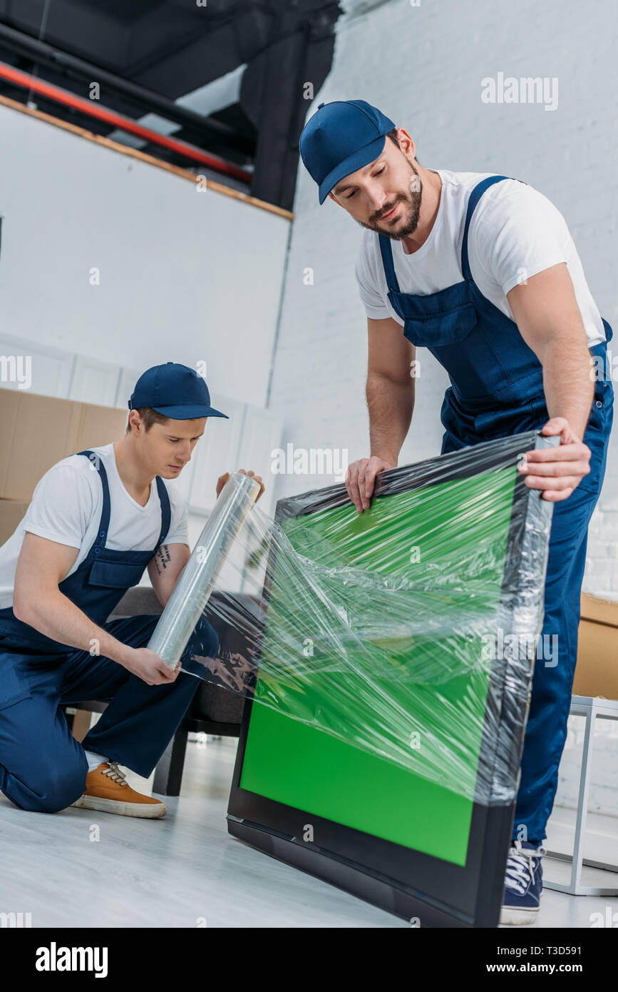 two movers using roll of stretch film while wrapping tv with green ...