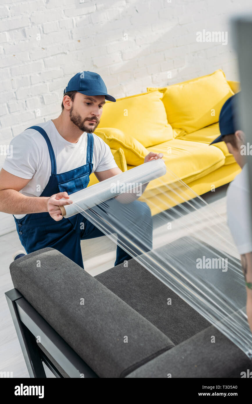 mover wrapping couch with roll of stretch film in apartment Stock Photo ...