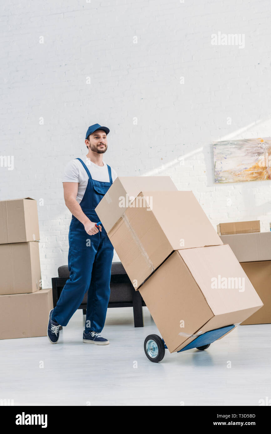 mover in uniform transporting cardboard boxes on hand truck in ...