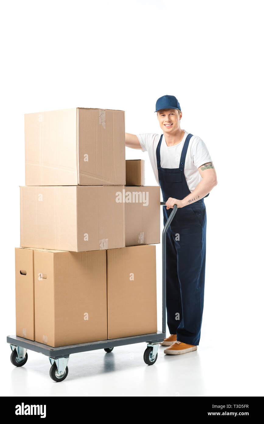 handsome mover in uniform smiling while transporting cardboard boxes on ...