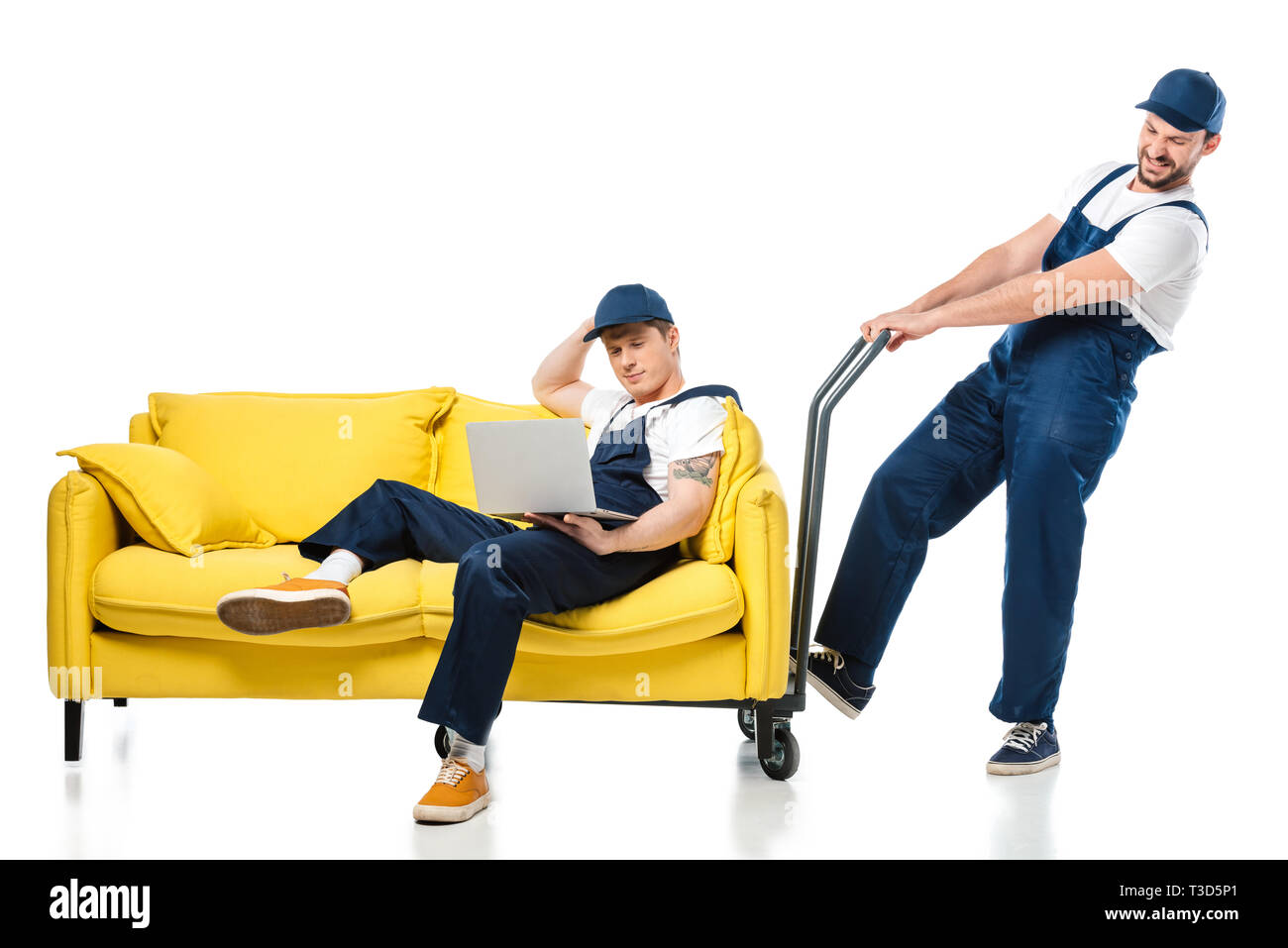 mover in uniform sitting on sofa and using laptop while colleague ...