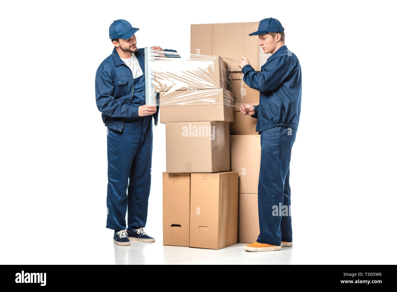 two movers wrapping cardboard boxes with roll of stretch film on white ...