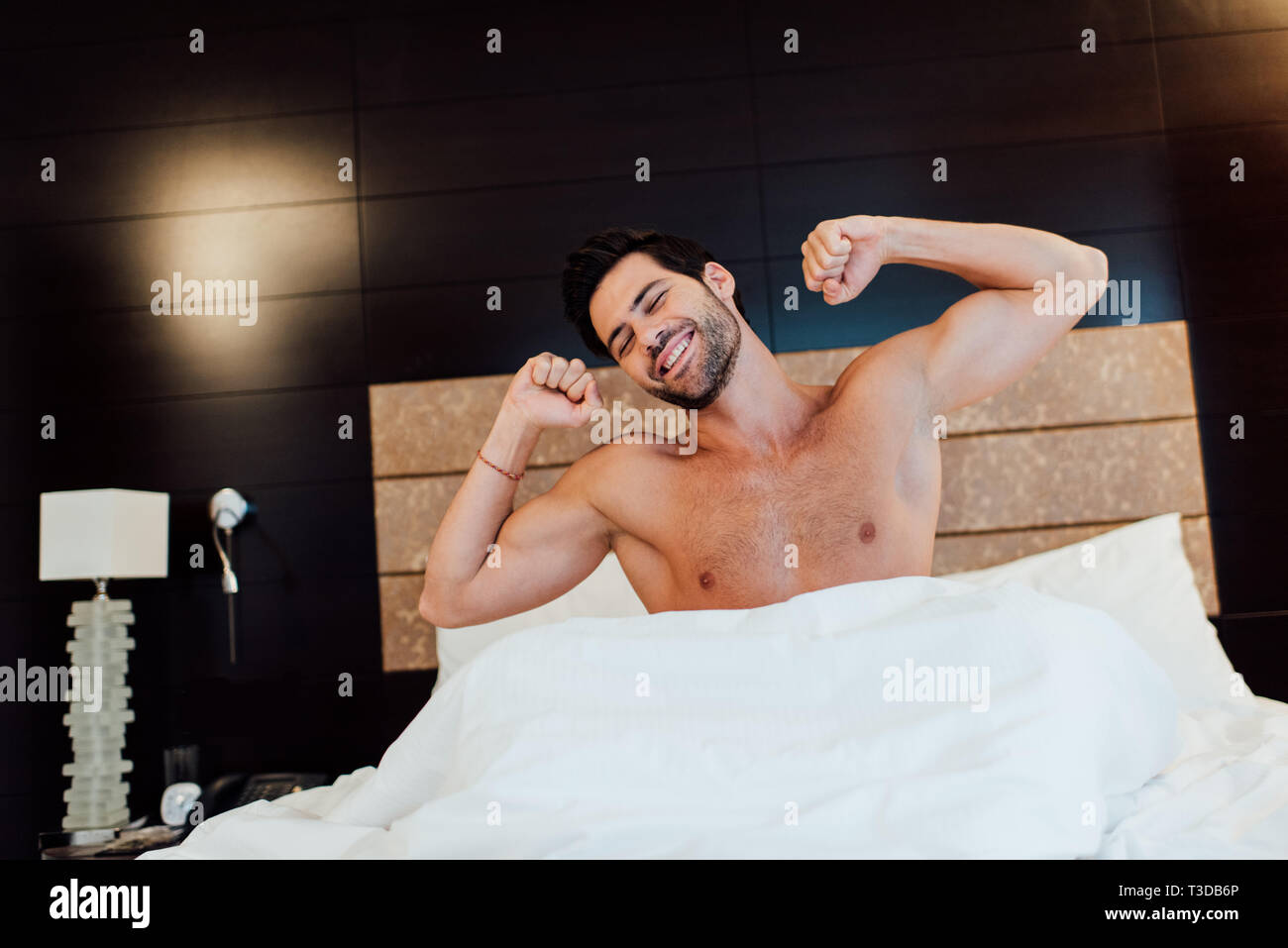 cheerful muscular man stretching in bed after wake up Stock Photo - Alamy