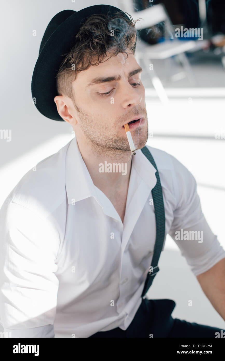 serious man in white shirt and black hat smoking cigarette Stock Photo ...