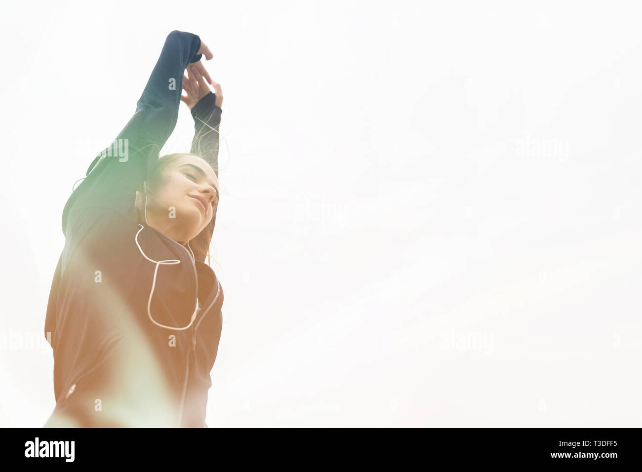 Female young athlete stretching her arms while listening to music ...