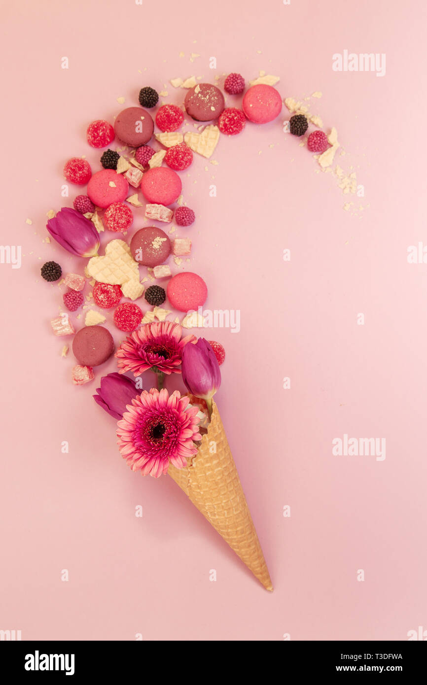 Mix of flowers and sweets in a waffle cone. Pink background, selective ...