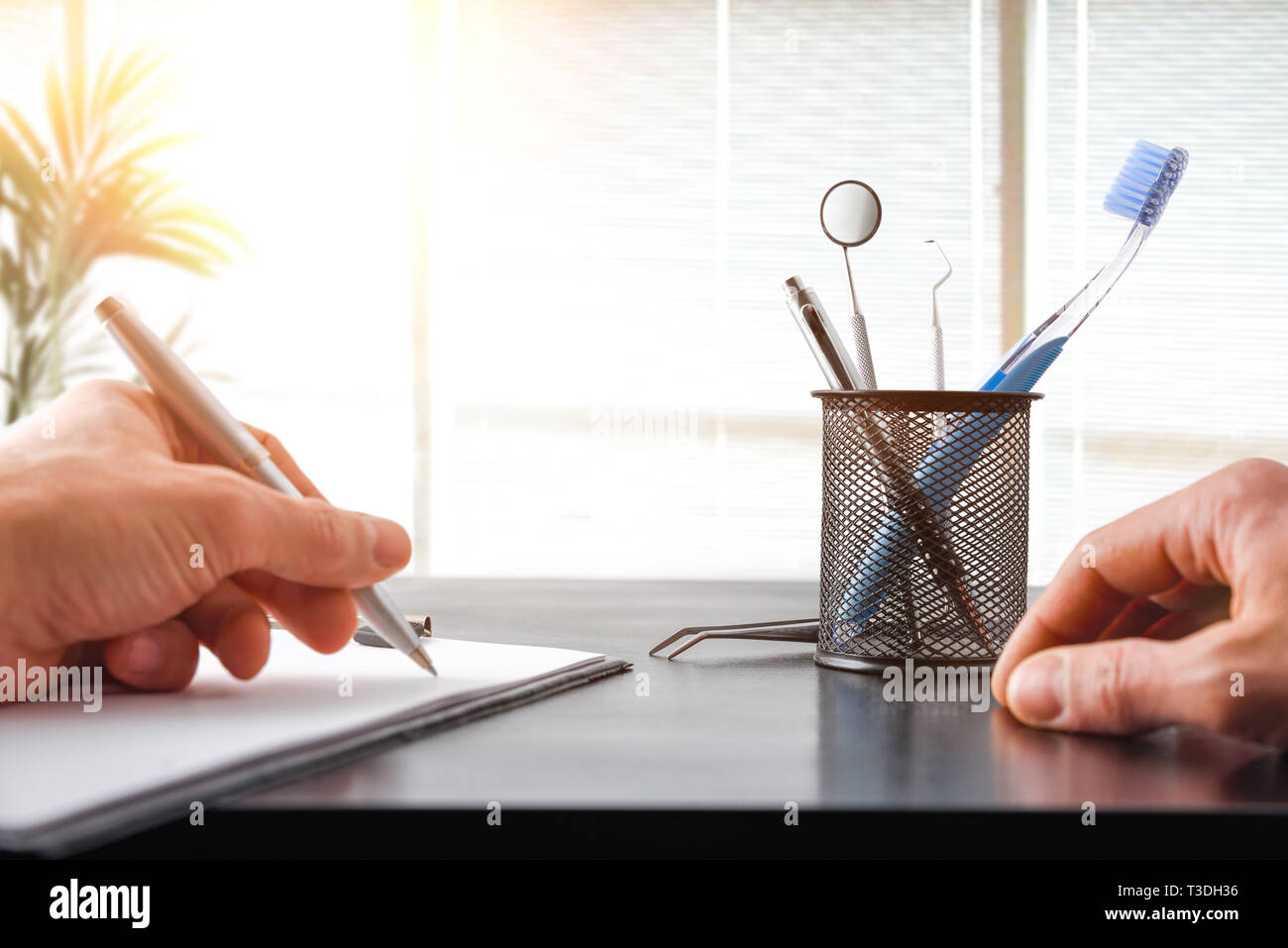 Dentist doctor writing on his desk with curtains and plant background ...