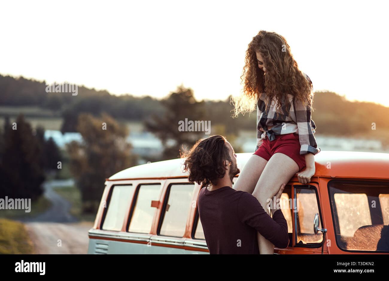 A young couple on a roadtrip through countryside, standing by minivan ...