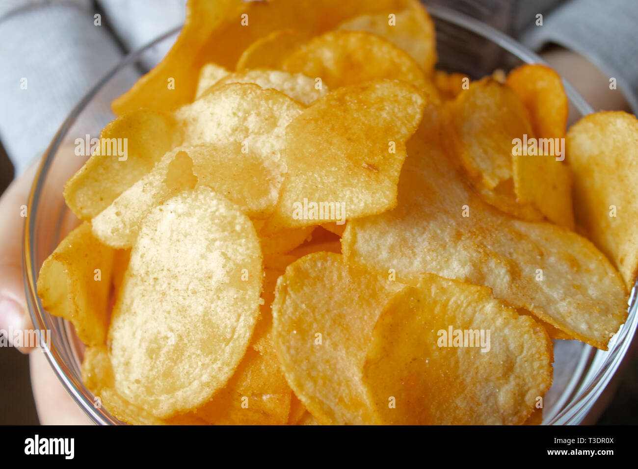Chips close-up, in a glass container. A child holds a bunch of yellow ...