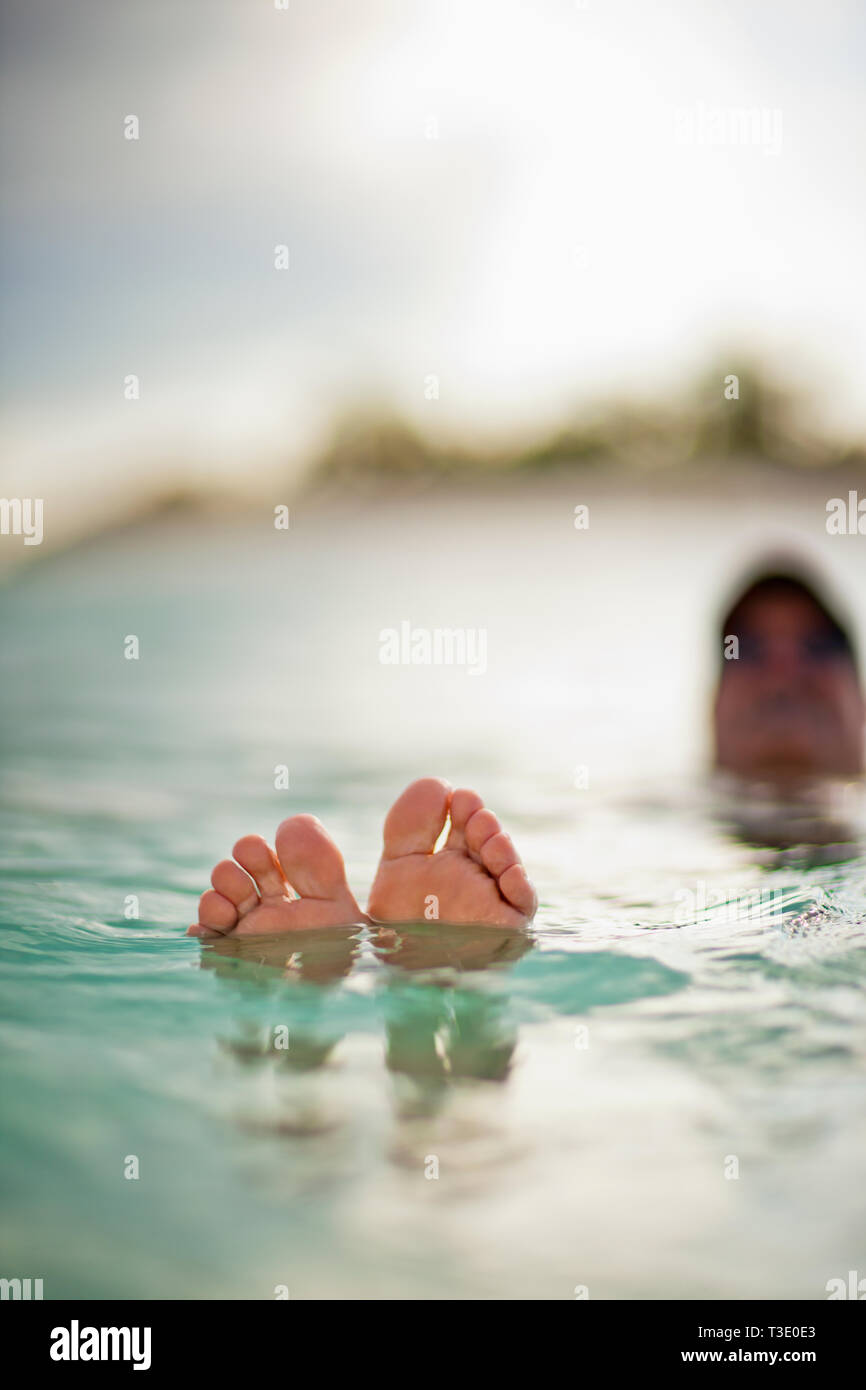 Toes poking up out of the water as a man floats in tropical ocean water ...