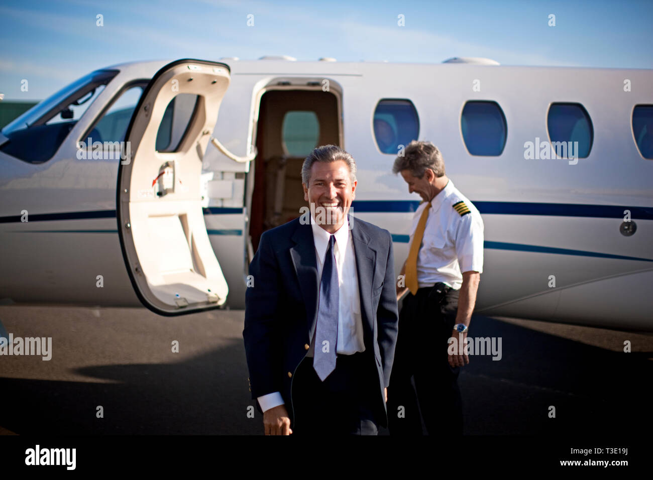 A businessman and a pilot standing in front of a private jet and ...