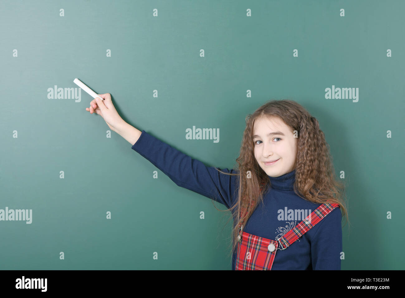 Schoolgirl near green school board. Young playful girl holds the chalk ...