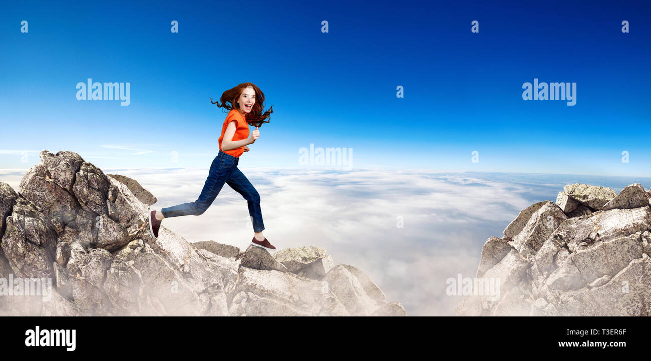 Redhead woman jumps over cliff on blue sky background Stock Photo - Alamy