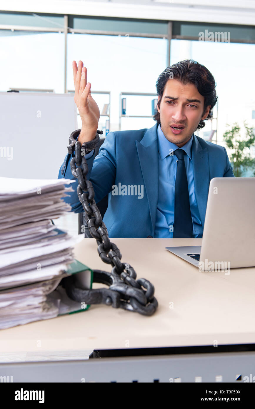 Chained male employee unhappy with excessive work Stock Photo - Alamy