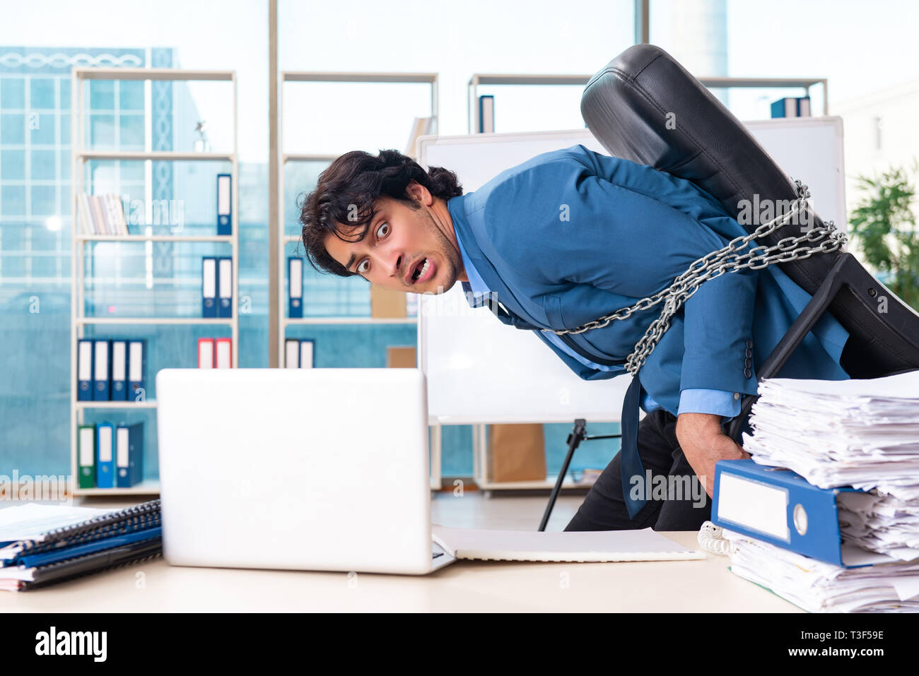 Chained male employee unhappy with excessive work Stock Photo - Alamy