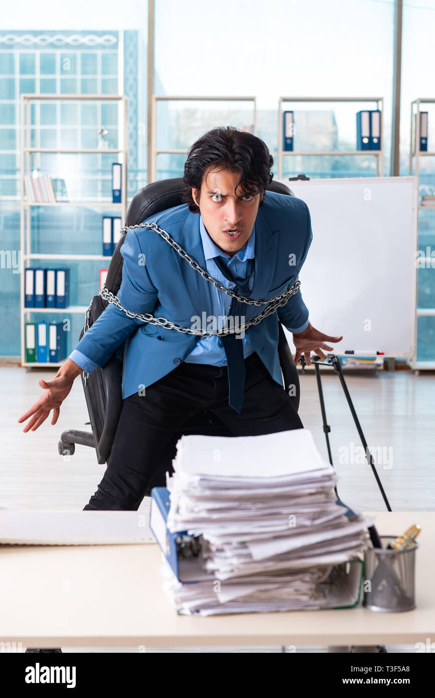 Chained male employee unhappy with excessive work Stock Photo - Alamy