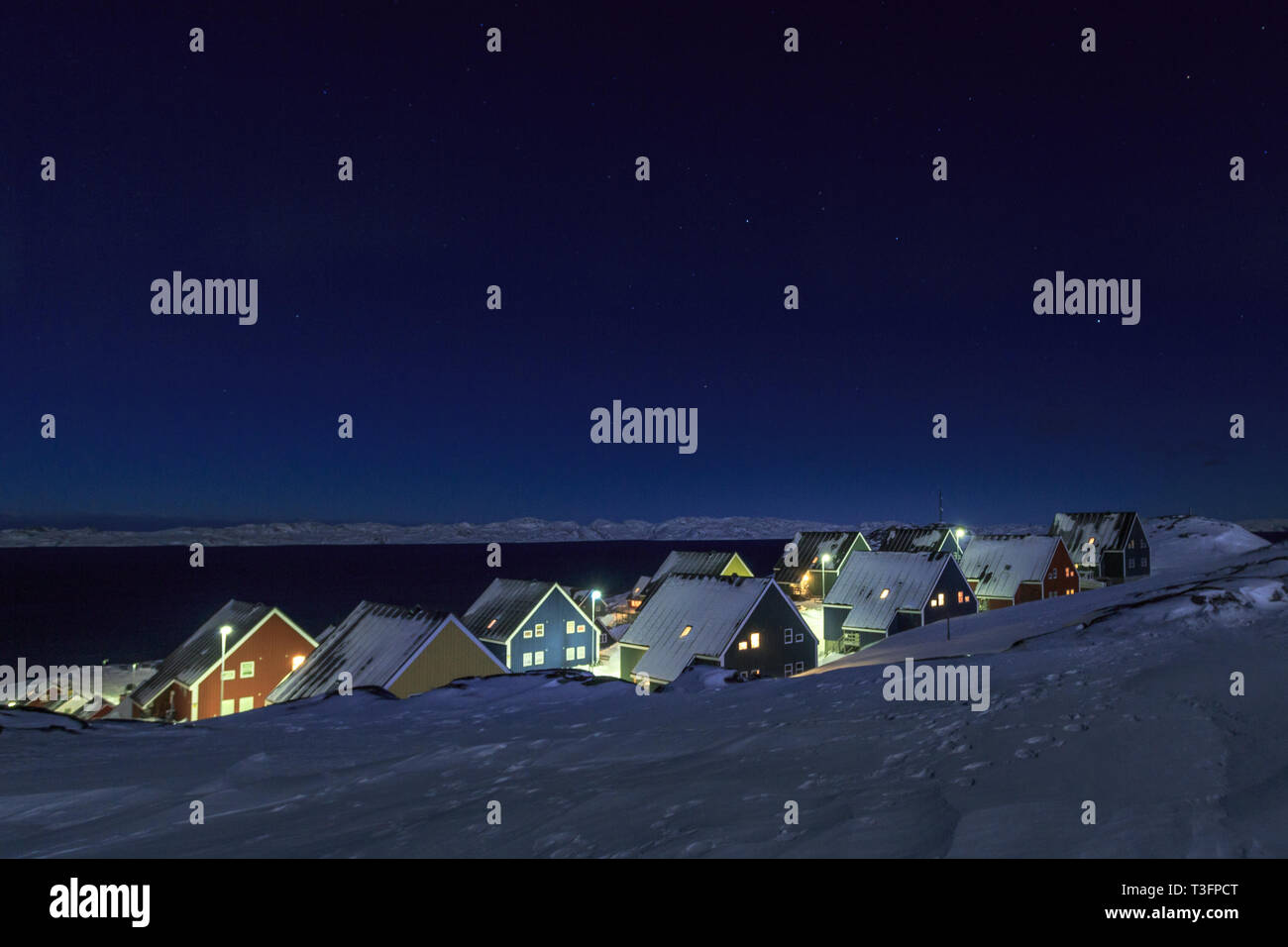 Yellow, blue, red and green inuit houses covered in snow at the fjord ...