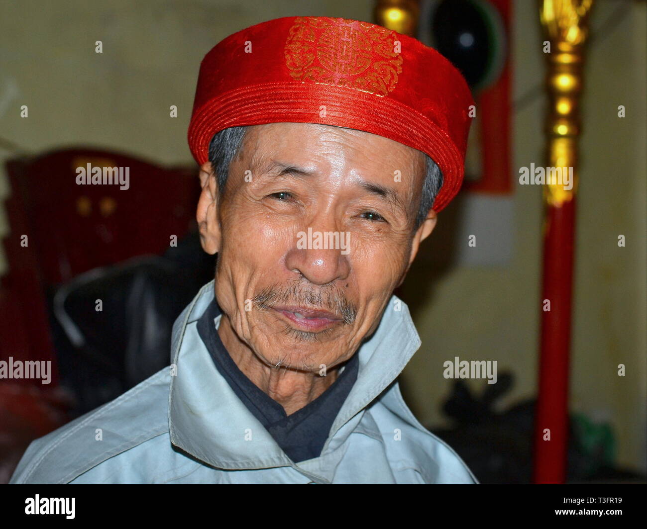 Elderly Vietnamese priest wears a distinctive red Taoist hat and poses ...
