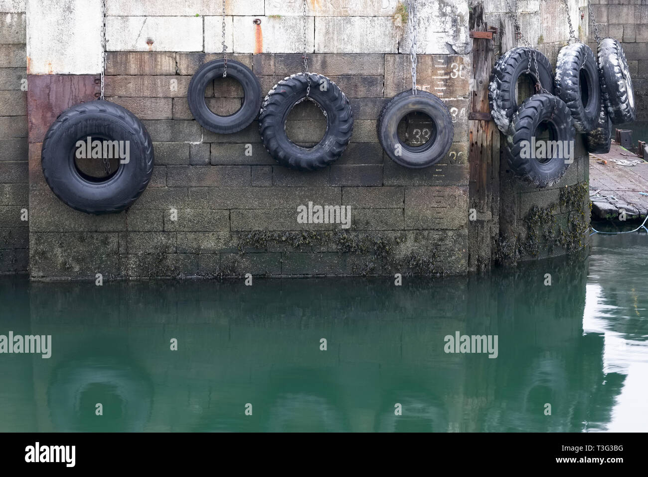 Car tyres hanging on rope against harbour wall at port dock to protect ...