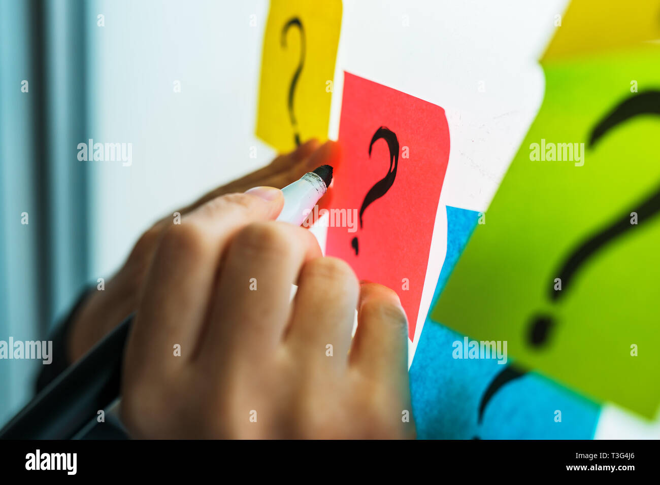 Businesswoman writing question marks on colorful sticky note paper on ...